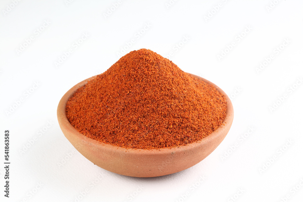Red chilli powder in a terracotta bowl placed on a white background ...