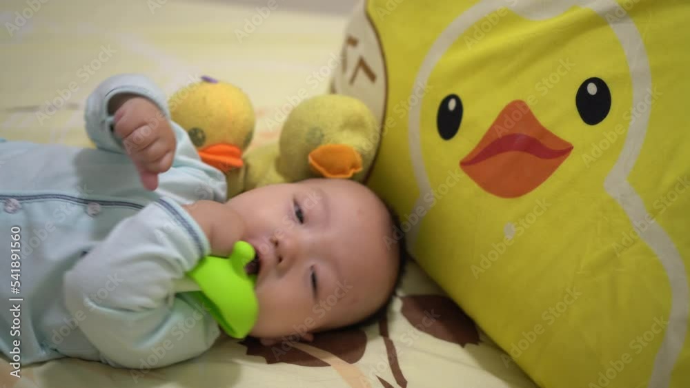 Cute Asian baby chew the teether toy at bed beside yellow duck plush ...