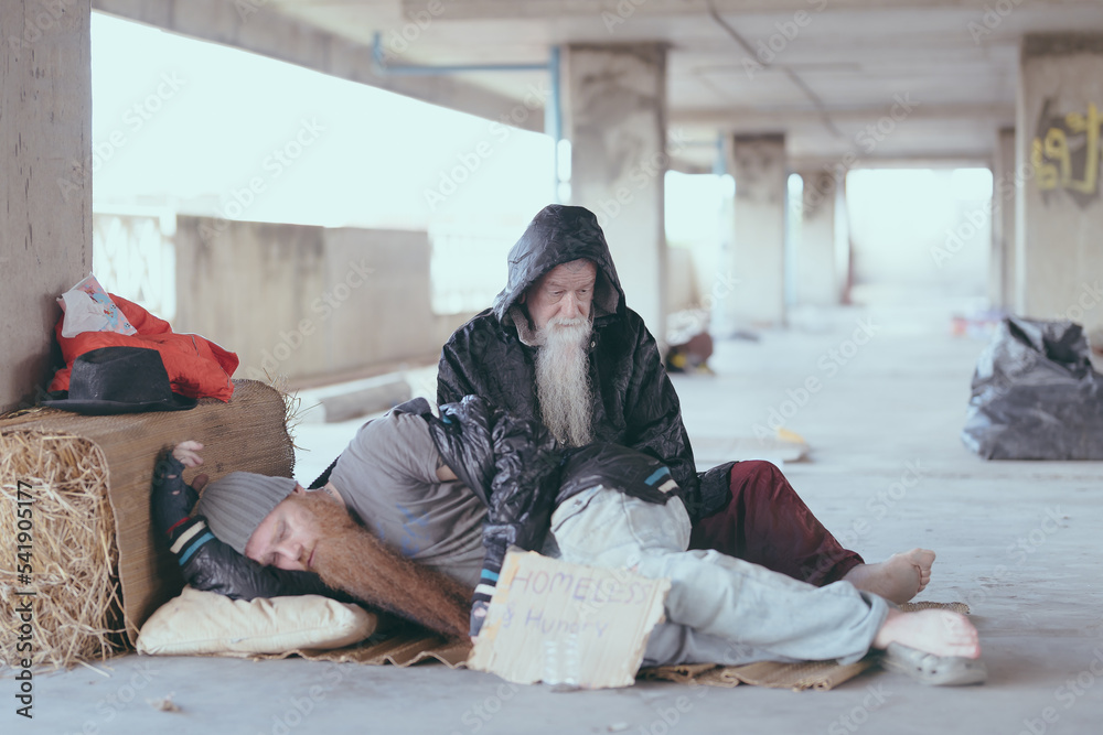 An old homeless man wearing a sweater and blanket sleeps on cardboard ...