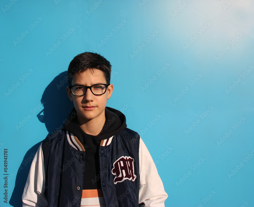 teenage boy in glasses standing on a blue background, smiling and ...