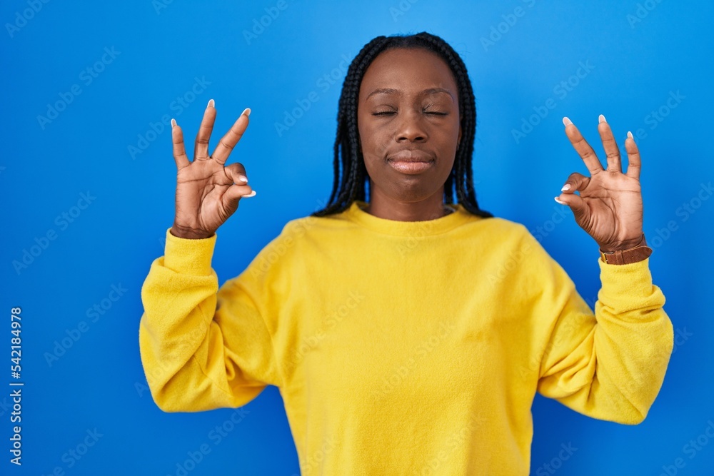 Beautiful black woman standing over blue background relaxed and smiling ...