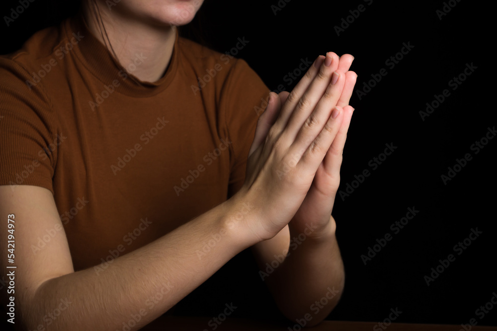 The girl folds her hands in prayer to God on a black background. prayer ...