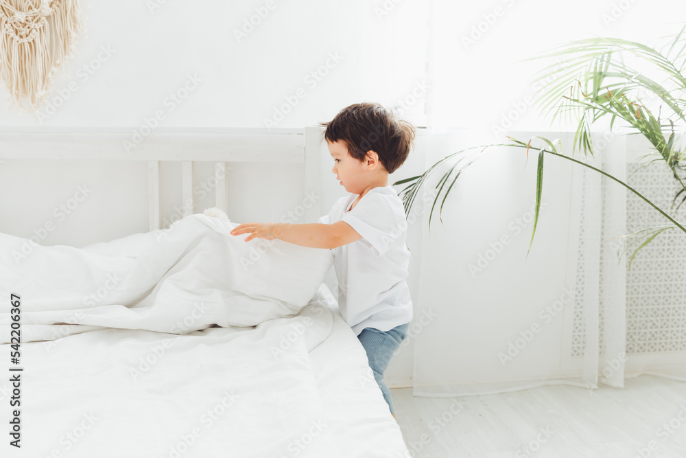 Happy little Asian boy cleans his room and folds a blanket in the ...