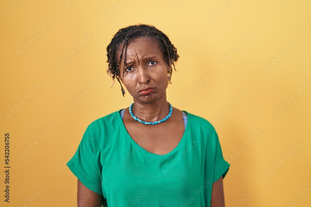 African woman with dreadlocks standing over yellow background depressed ...