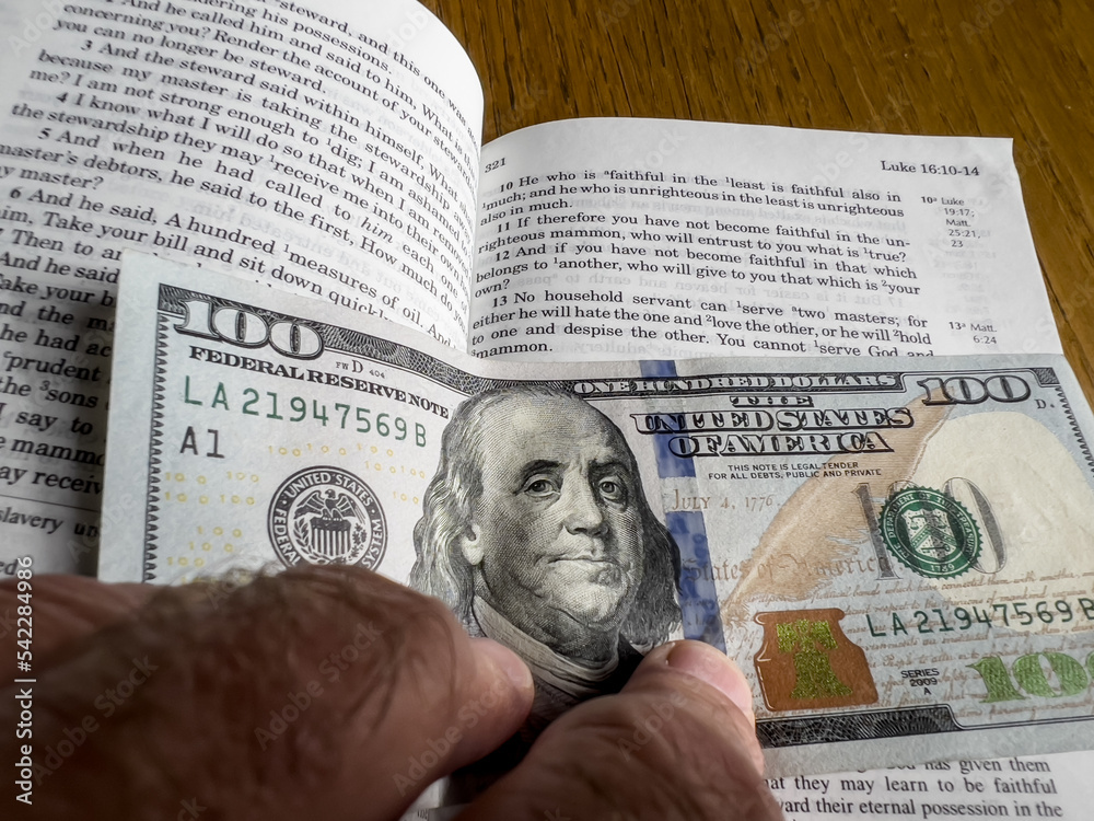 The Holy Bible in English with a tab from the US $ 100 banknote showing ...
