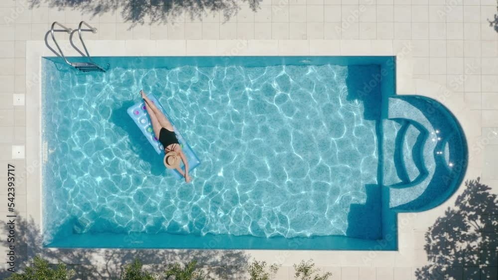 Top view swimming pool with relaxing woman in black swimsuit, straw hat ...
