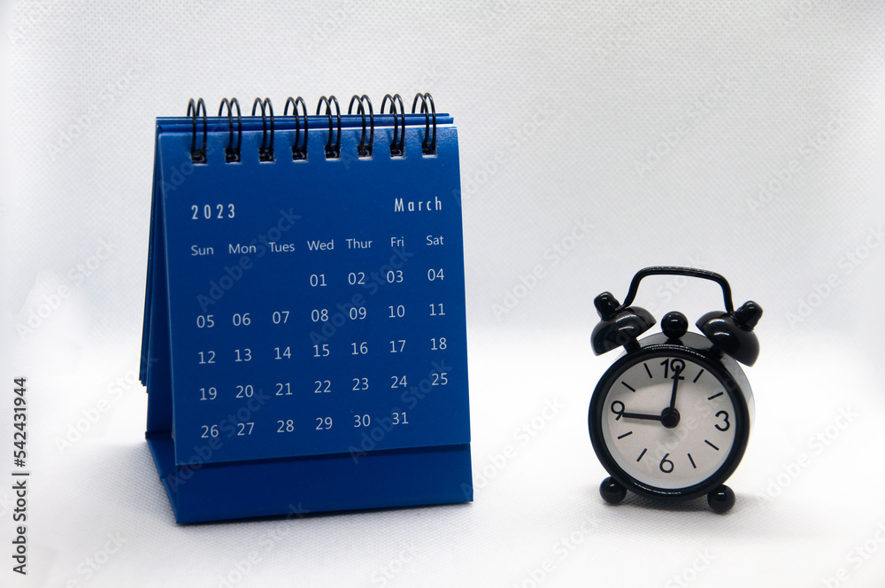 Alarm clock pointing at 9 o'clock with March 2023 calendar on white ...