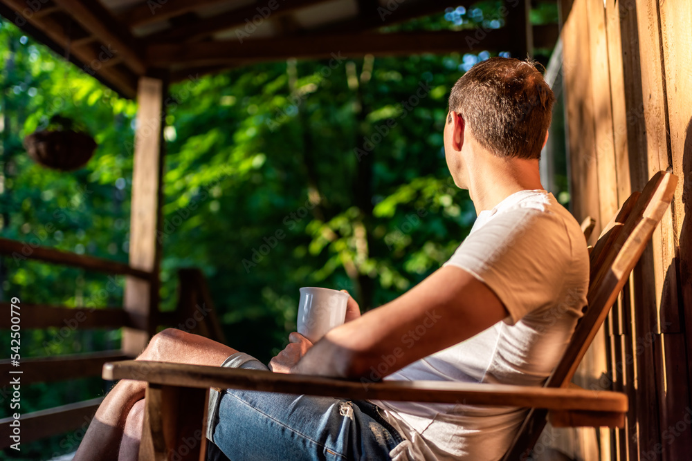 Man sitting on rocking chair on porch of rustic countryside home house ...
