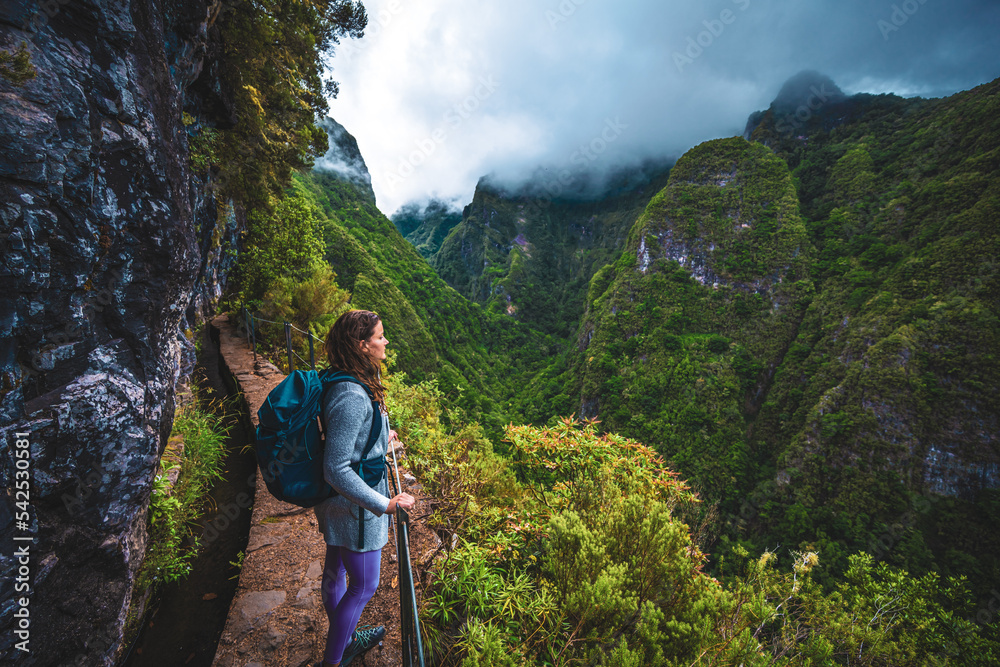 Beautiful woman admires the view from the adventurous cliff jungle path ...