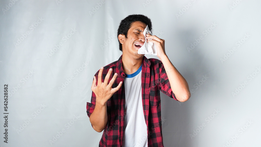 Asian Man Wearing Red Flannel Tshirt Cry Using A Tissue Isolated White