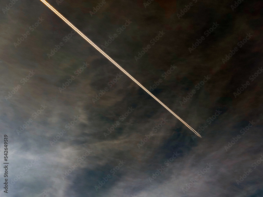 A long white trail from a flying plane. In the dark night sky with ...