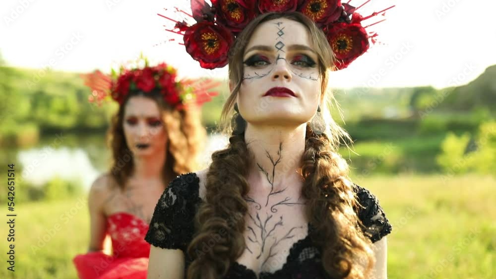 Beautiful women witches in long red and black dresses flowers hoop walk ...