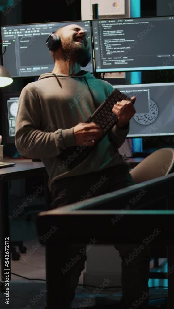 Vertical video: Young programmer playing air guitar in agency office, enjoying music and song ...