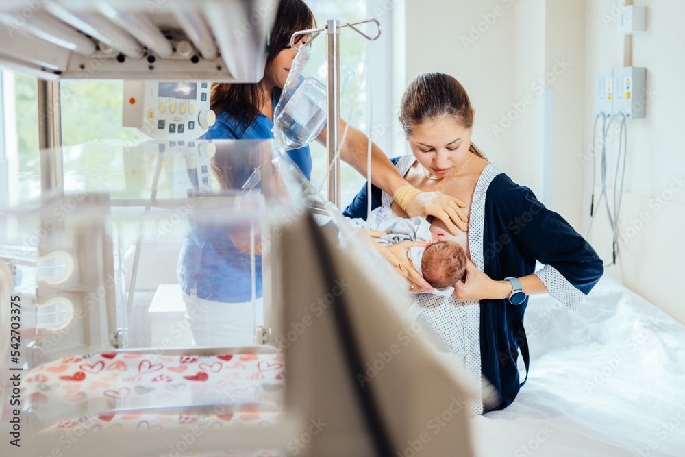 Female nurse assisting young woman in breast feeding baby in hospital ...