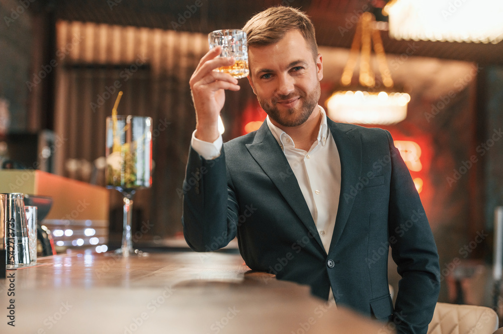 Sitting by the table. An elegant man in black suit is in the bar ...