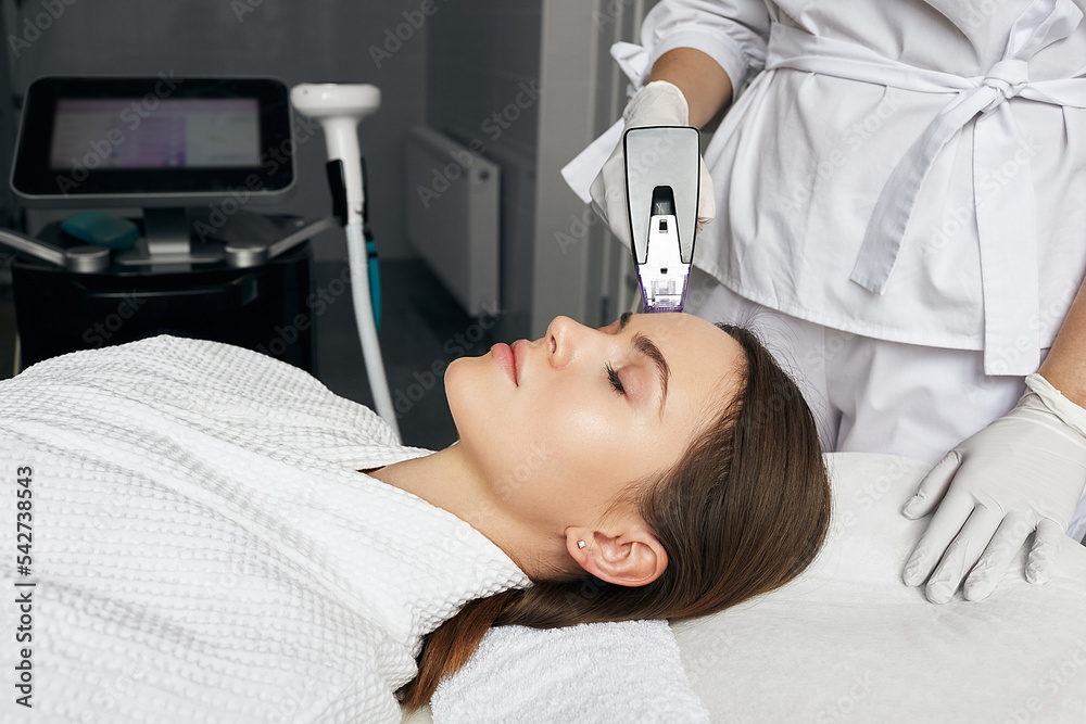 Pretty woman enjoying radiofrequency lifting procedure for her face and forehead skin ...