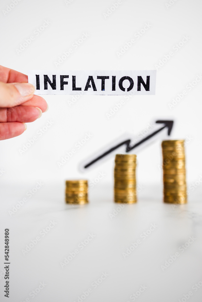 hand holding inflation text in front of growing stacks of coins with ...