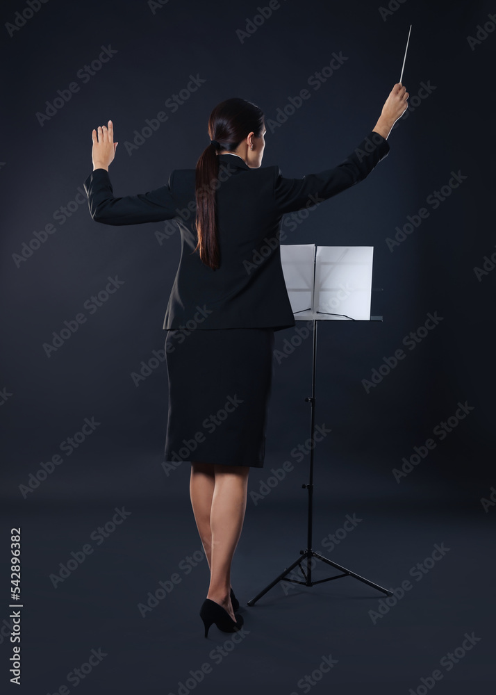 Professional conductor with baton and note stand on dark background ...