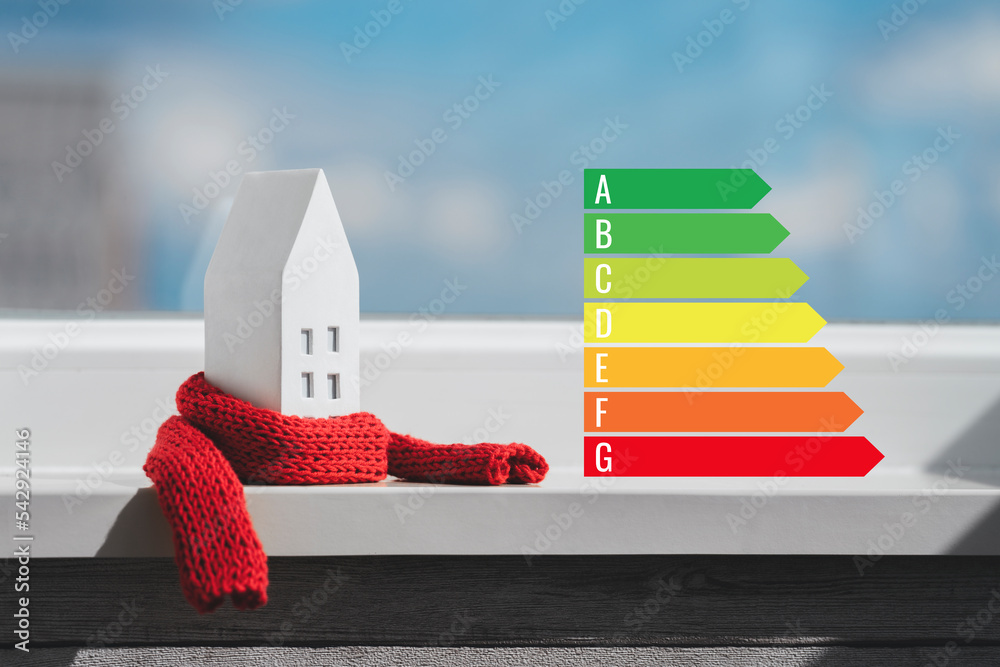 Miniature house in a red scarf and energy efficiency chart on the ...
