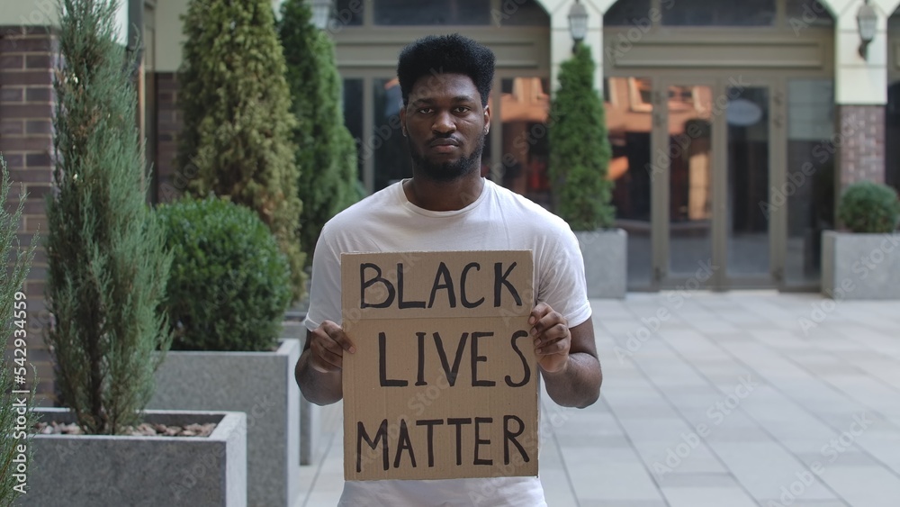 Young African American man stands with a cardboard poster RACISM IS A ...