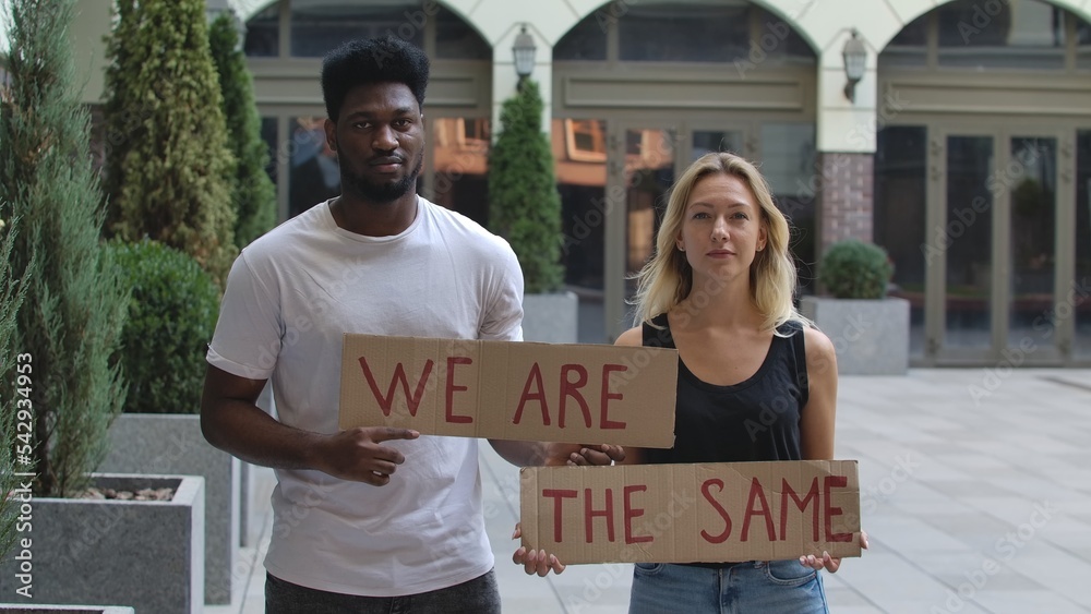 Black man and white woman stand on the street holding posters for WE ...