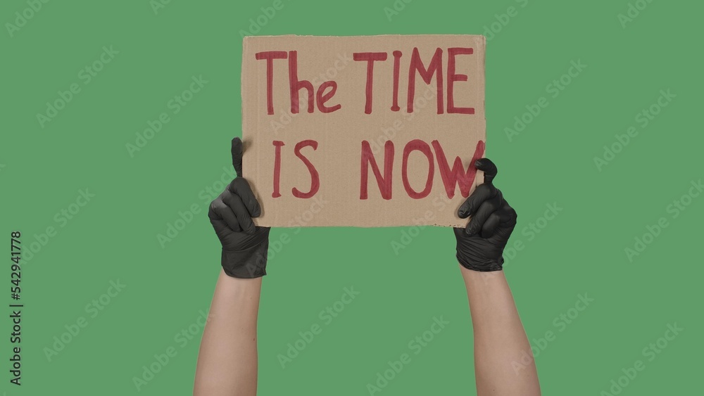 Hands in black gloves raising up cardboard poster THE TIME IS NOW. Stop ...