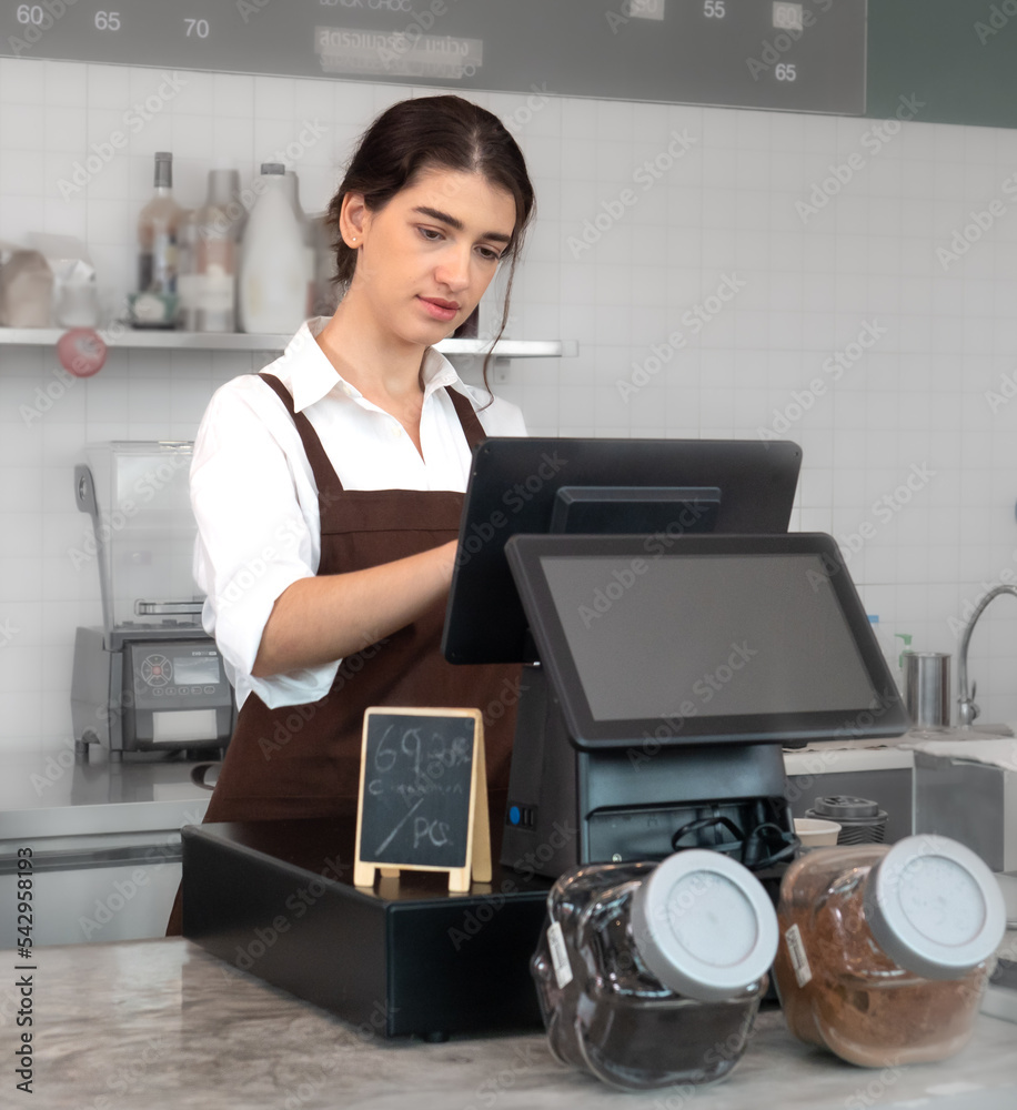 Beautiful female cashier standing at counter working with cash register ...