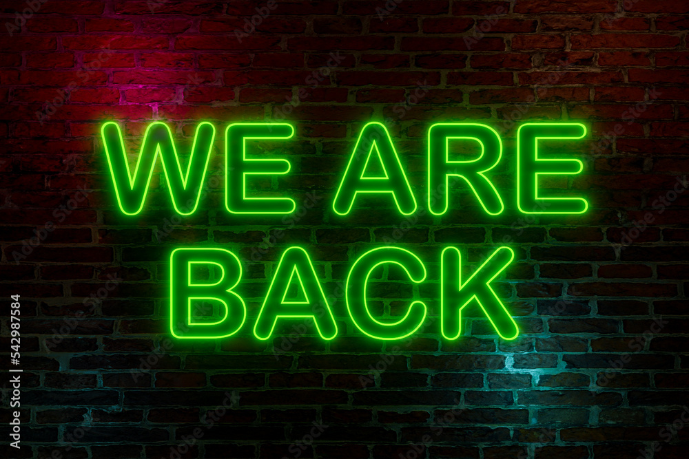We are back, neon sign. Brick wall at night with the text "We are back ...