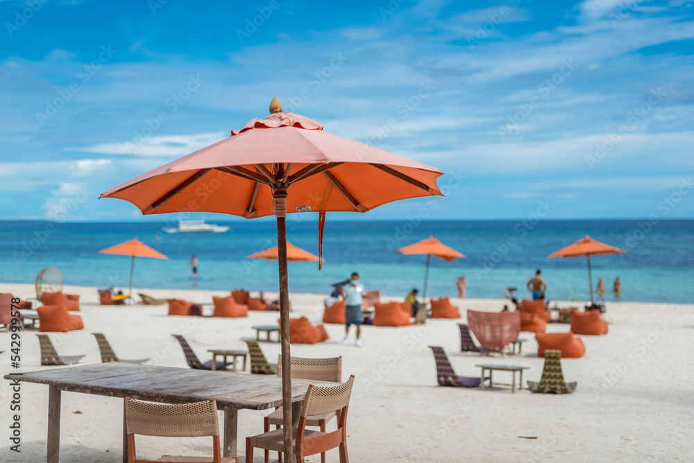 Orange wicker rattan chairs and matching parasols dot the beachfront of ...