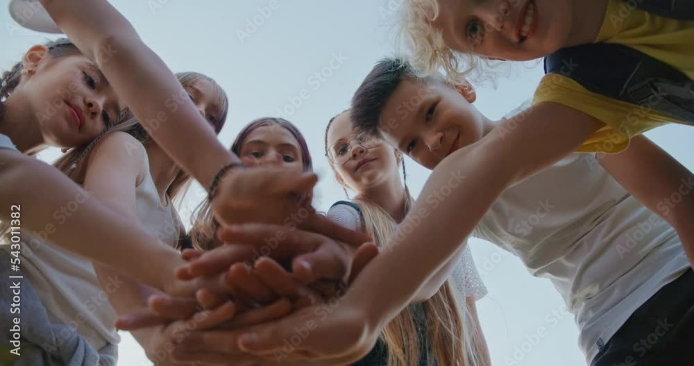 Close up of group of kids putting hands together, raising up on sky ...