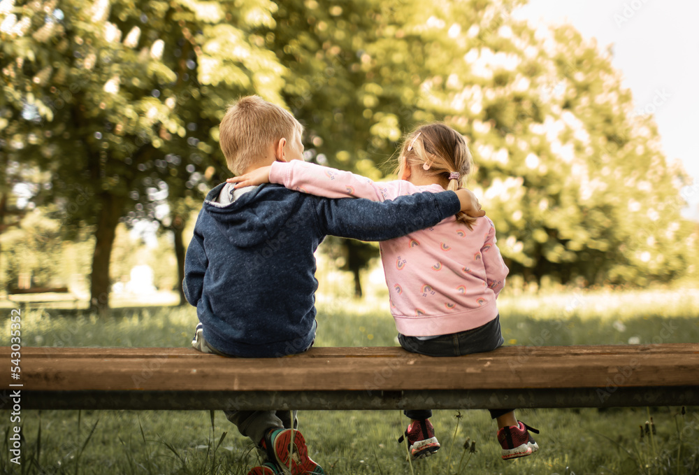 Little brother and sister giving a hug, girl and boy sitting on park ...