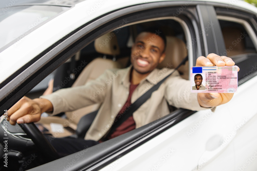 Happy young african man showing his driver's license from open car ...