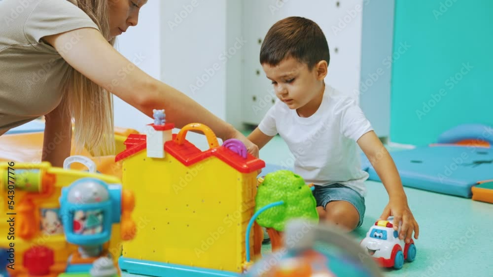 Little white boy in nursery playing with colorful toy car and toy house ...