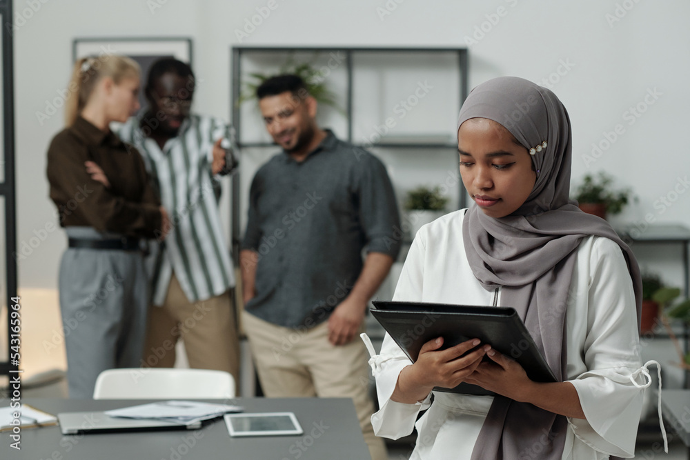 Young Muslim businesswoman in hijab holding black folder with documents ...