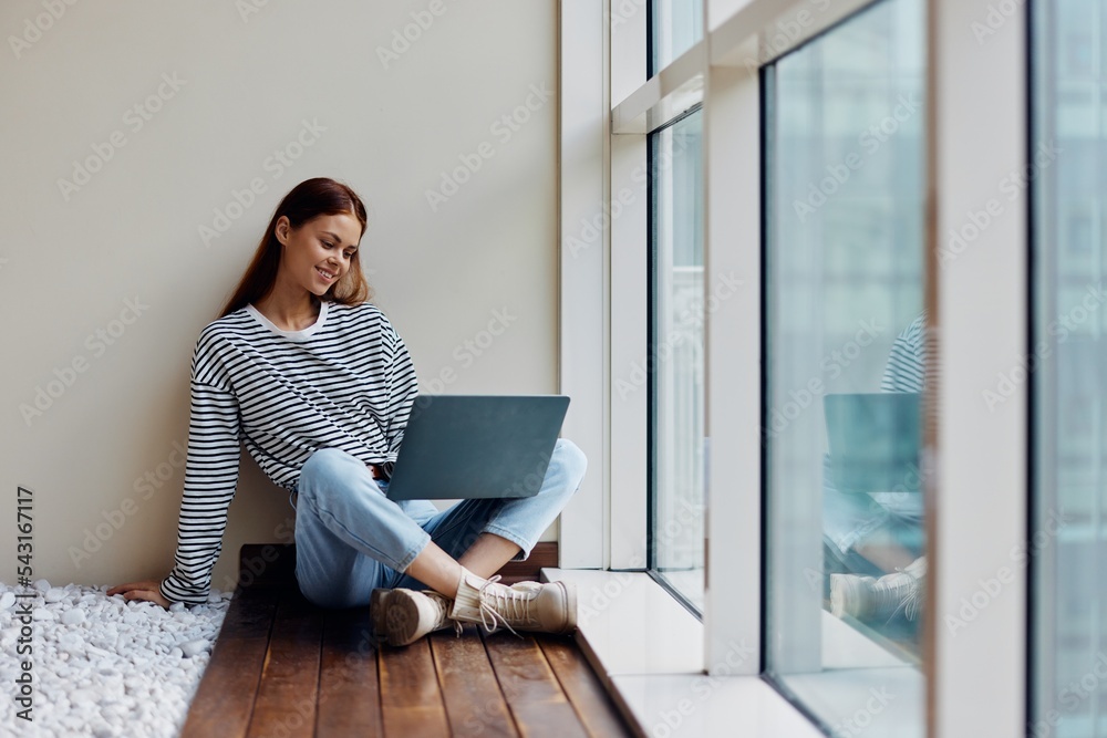 Business woman sitting with a laptop at the window full-length and ...