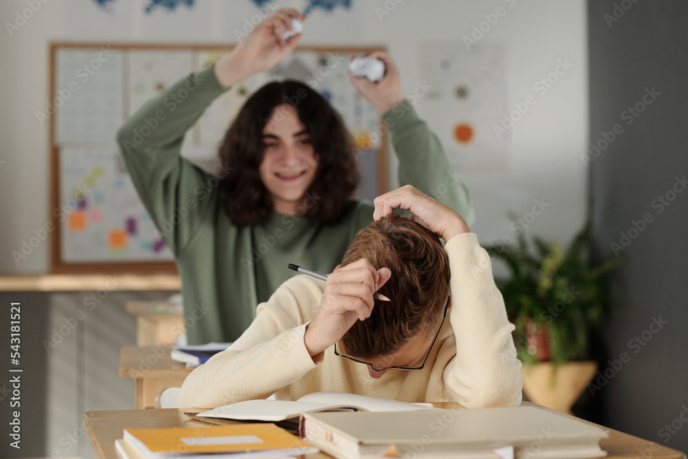 Youthful schoolboy bending over desk and covering his head by hands ...