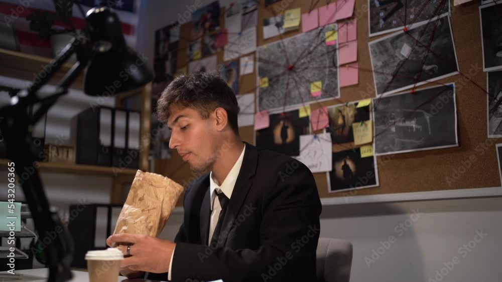 Detective eating hamburger in his office, private detective looking at ...