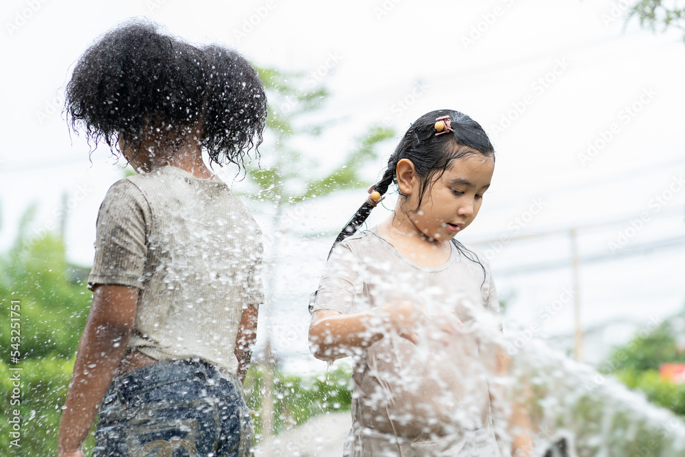 African American child girl and Asian child girl playing wet mud puddle ...