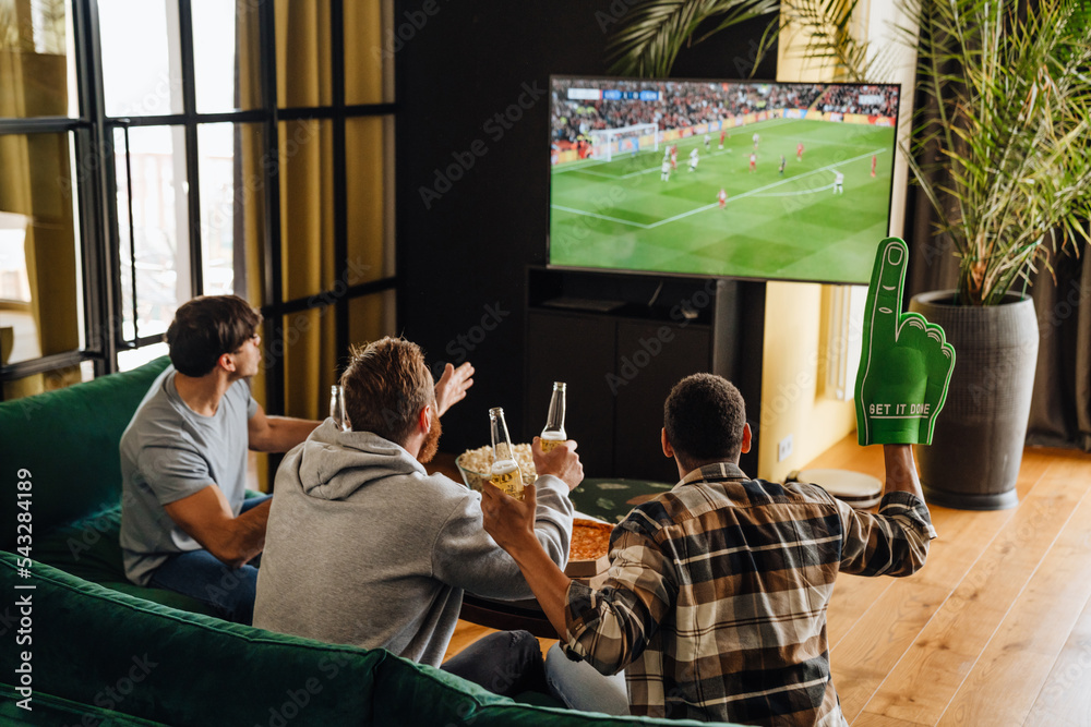 Back view of male friends watching football match while sitting in ...