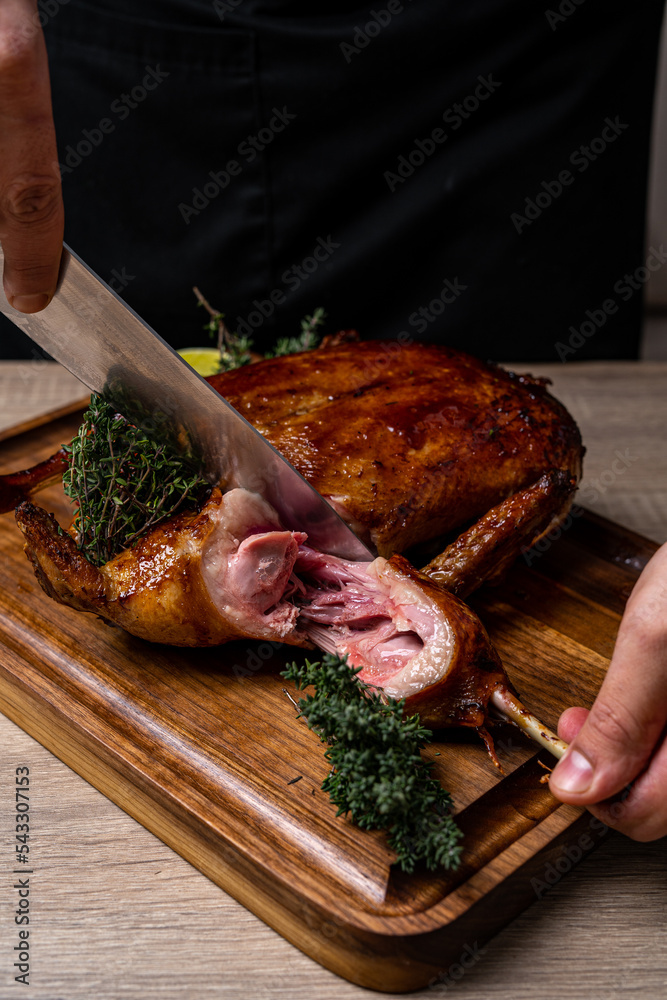 The hands of the cook cut the grilled baked duck on a wooden board ...
