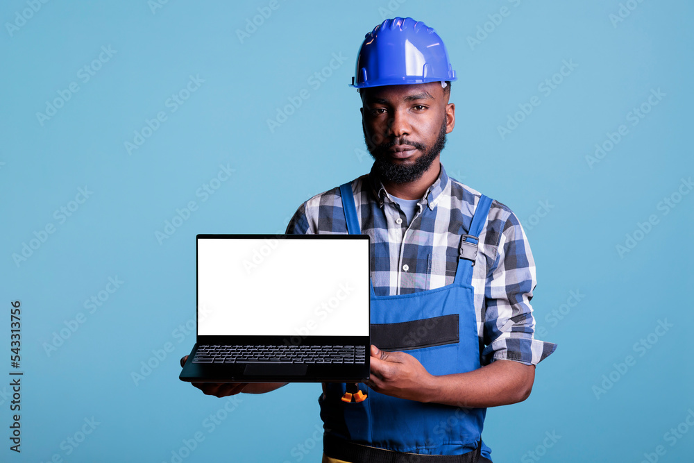 Serious builder looking at camera holding laptop with blank screen for ...