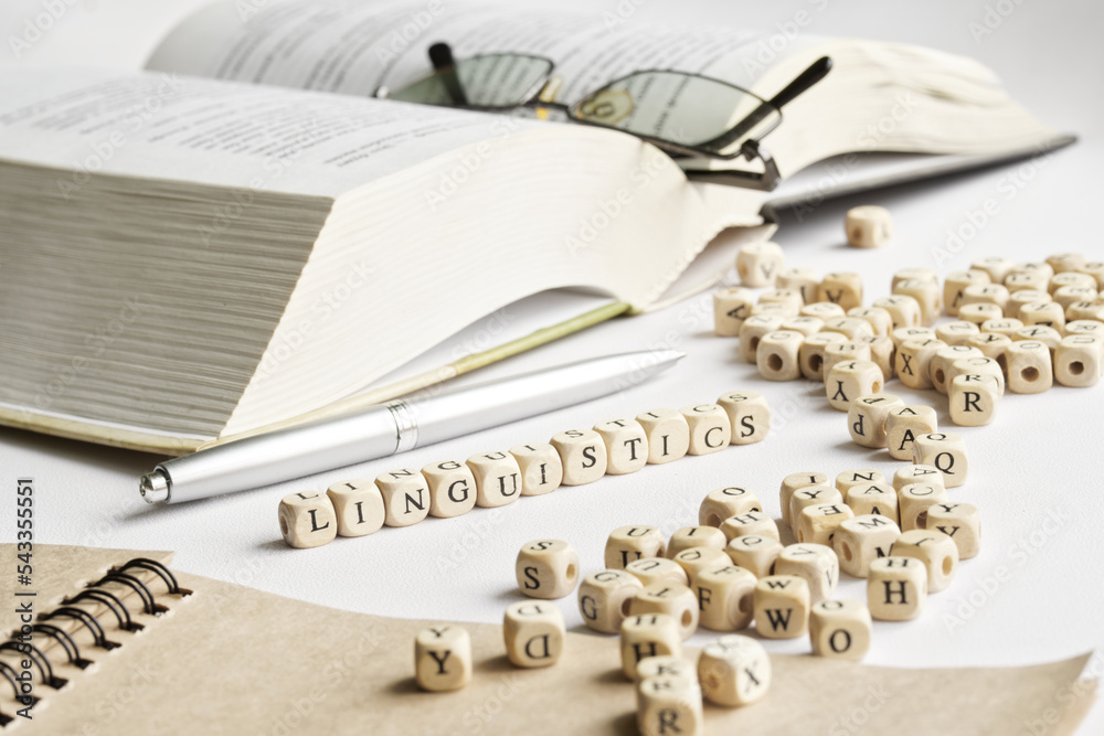 Word linguistics next to open book, glasses, notepad, pen and many letters. Concept of modern ...