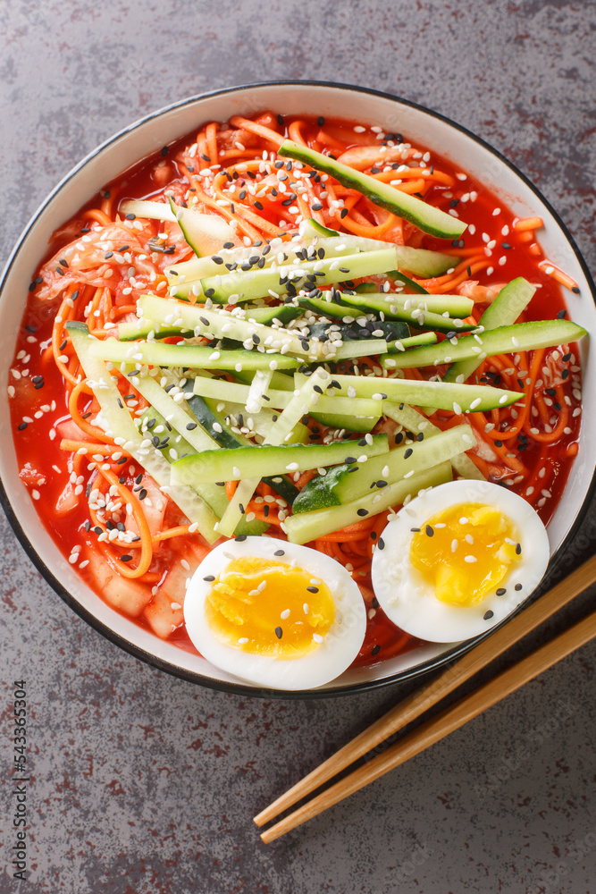 Korean cold noodle salad or bibim guksu, topped with boiled egg, sesame and cucumber closeup in ...