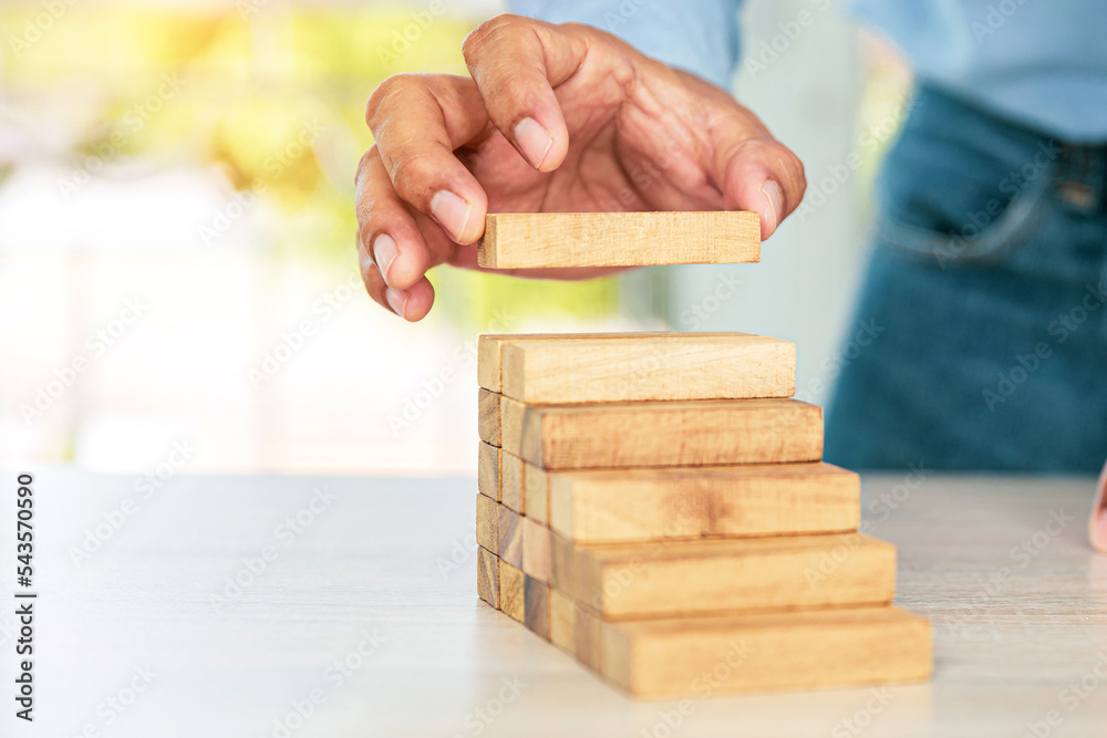 Hand placing wooden block tower stack in pyramid stair step with ...