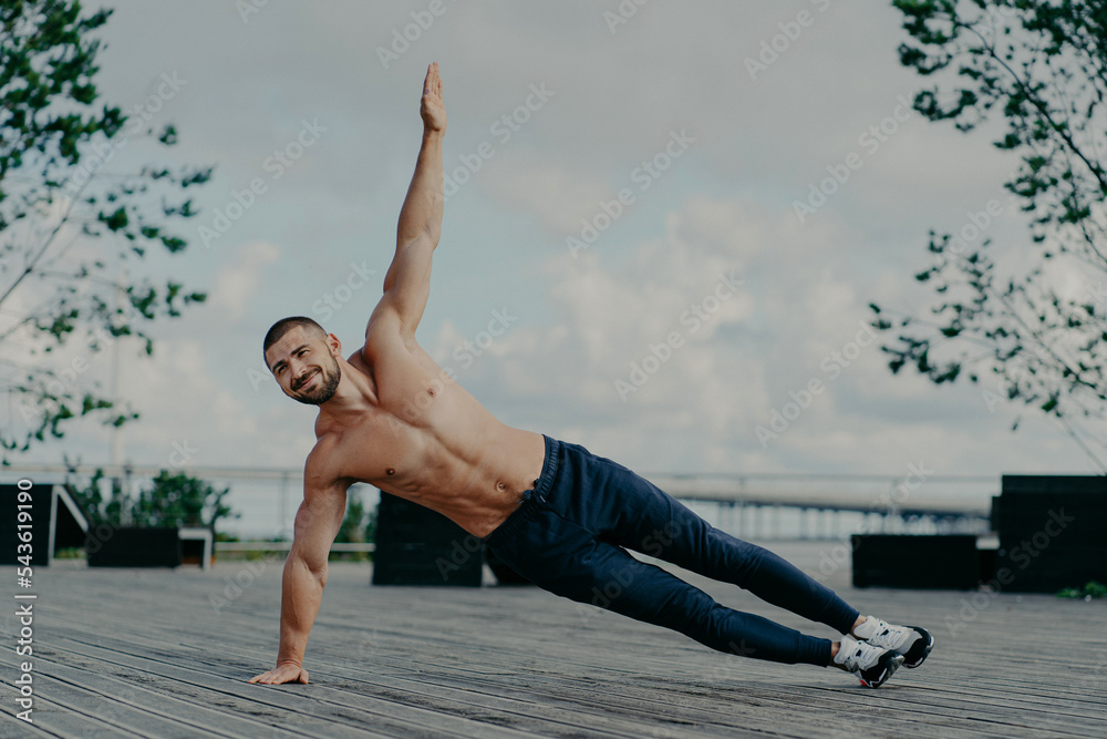Healthy man stands in abs side plank and raises arm, does exercises ...