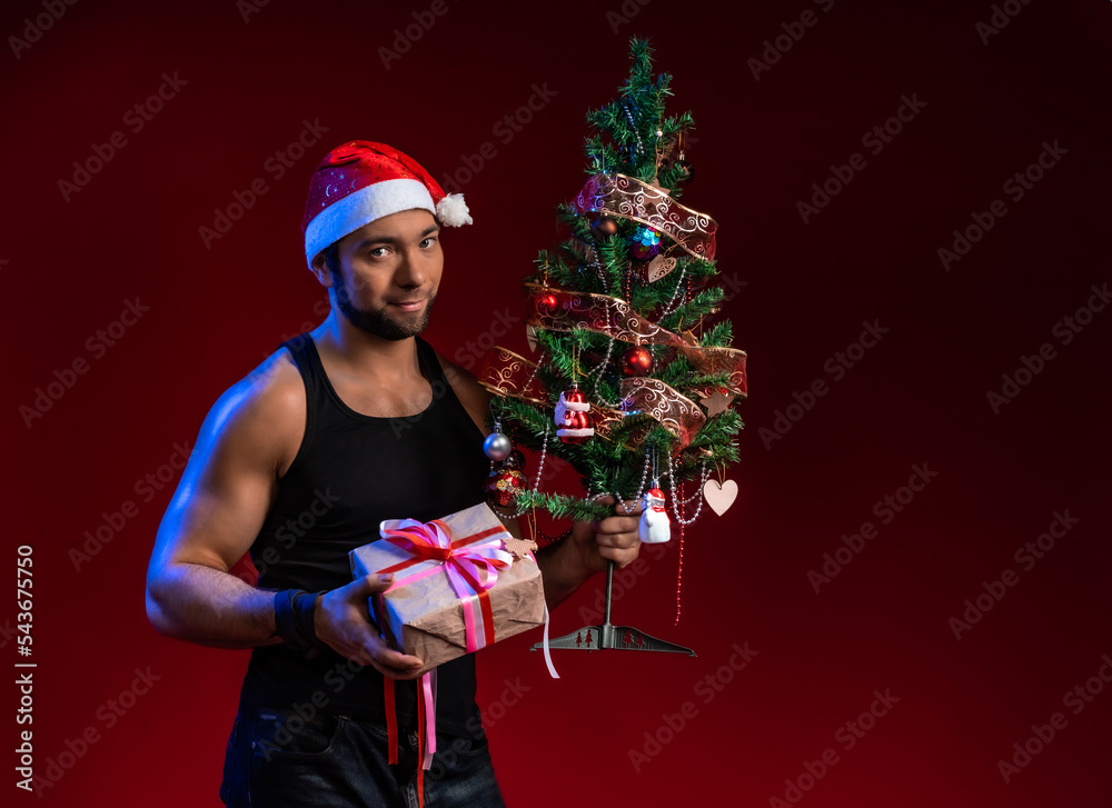 muscular man with a Christmas tree. sportsman posing in black t-shirt ...