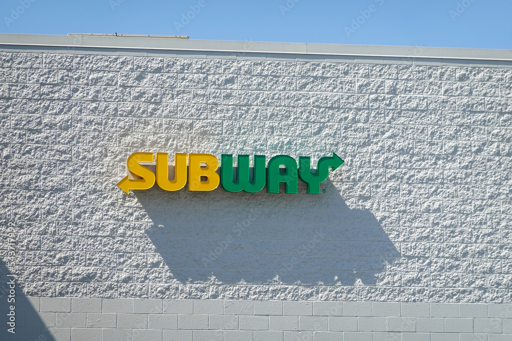 The sign for Subway sandwich shops on a white brick wall Subway is a ...