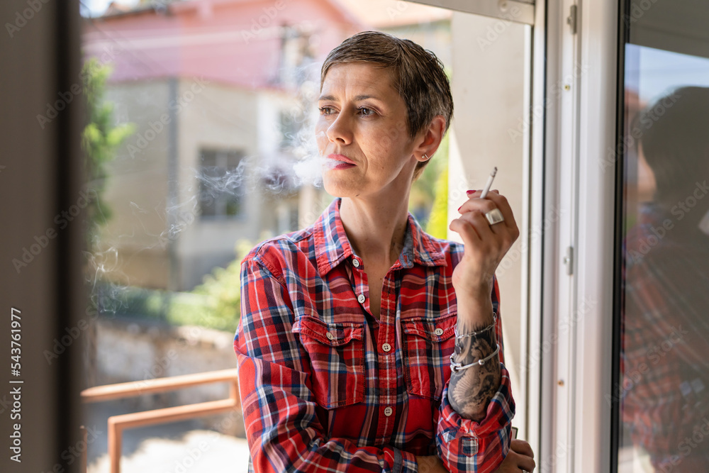 One woman mature or senior female smoking cigarette by the window at ...