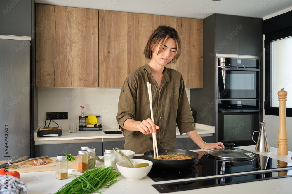 Smiley asian young man cooking chinese or taiwanese tomato scrambled ...