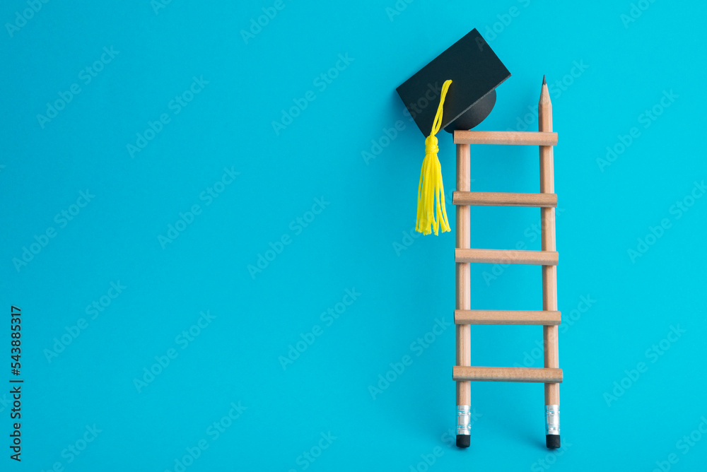 Graduation cap on top of pencil ladder with blue background copy space ...